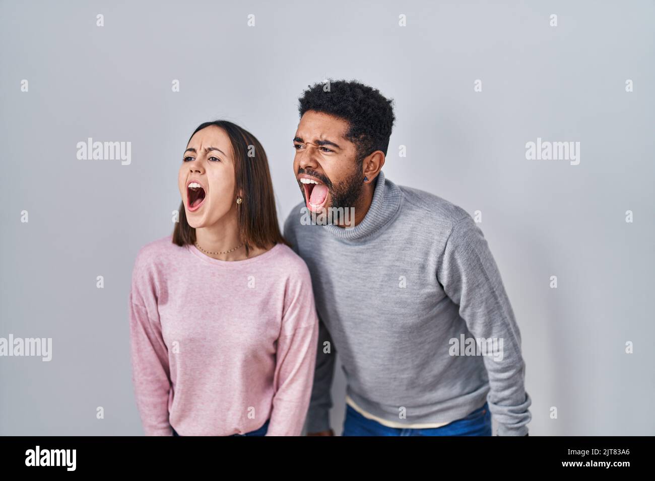 Young hispanic couple standing together angry and mad screaming ...