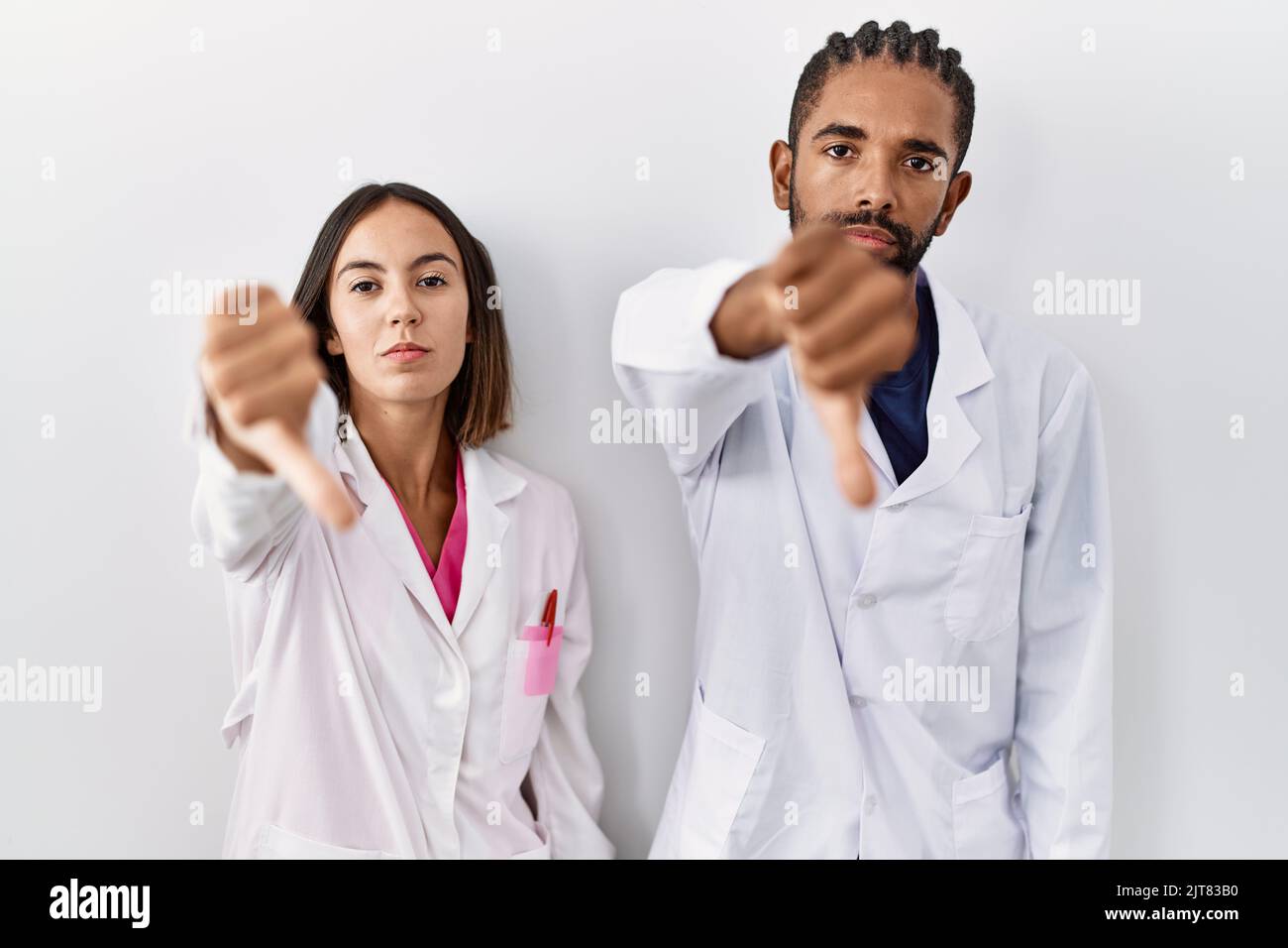 Young hispanic doctors standing over white background looking unhappy ...