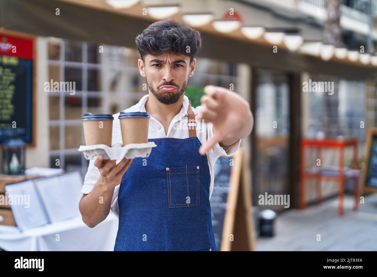 Arab man with beard wearing waiter apron at restaurant terrace with ...
