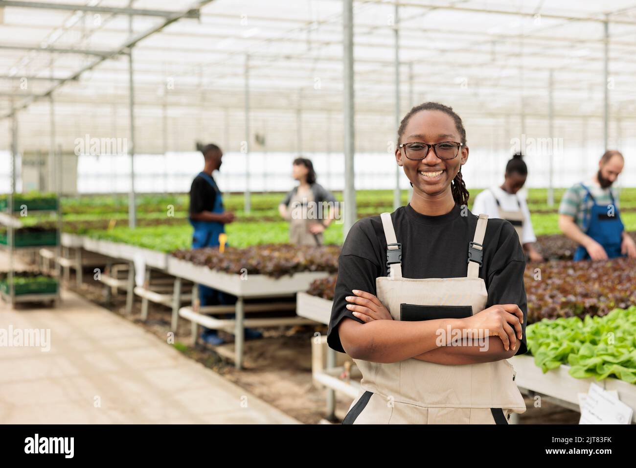 Portrait of smiling woman in modern greenhouse with workers taking care ...