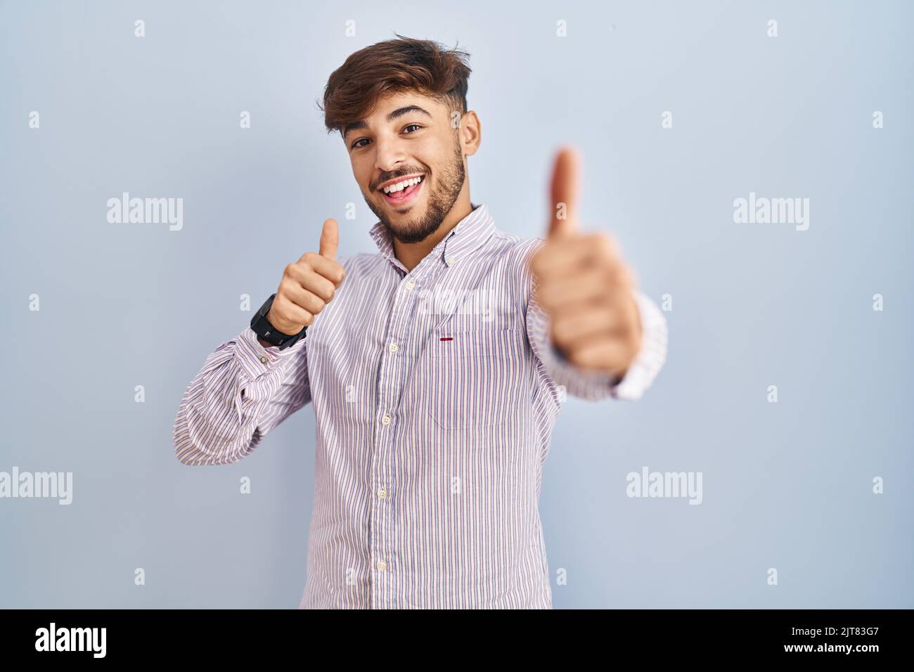 Arab man with beard standing over blue background approving doing ...
