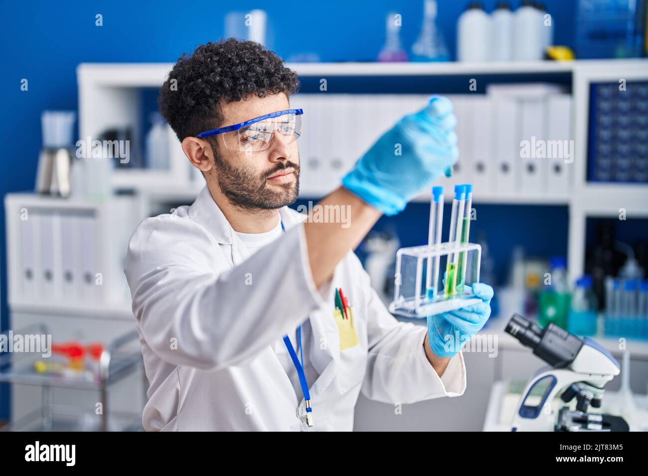 Young arab man wearing scientist uniform holding test tubes at ...
