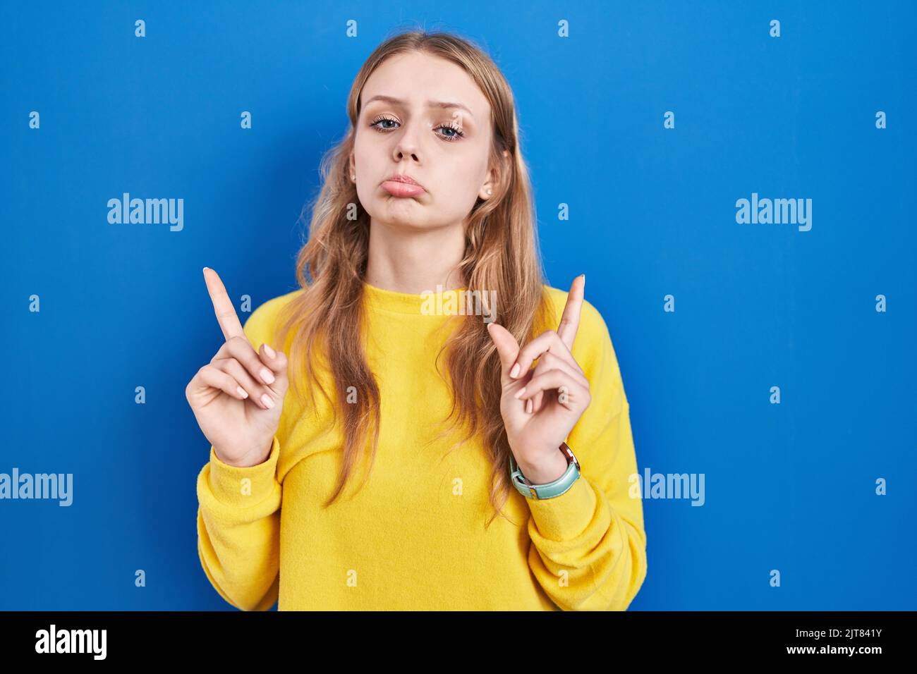 Young caucasian woman standing over blue background pointing up looking ...