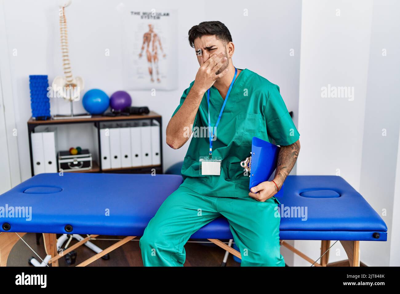 Young physiotherapist man working at pain recovery clinic smelling ...