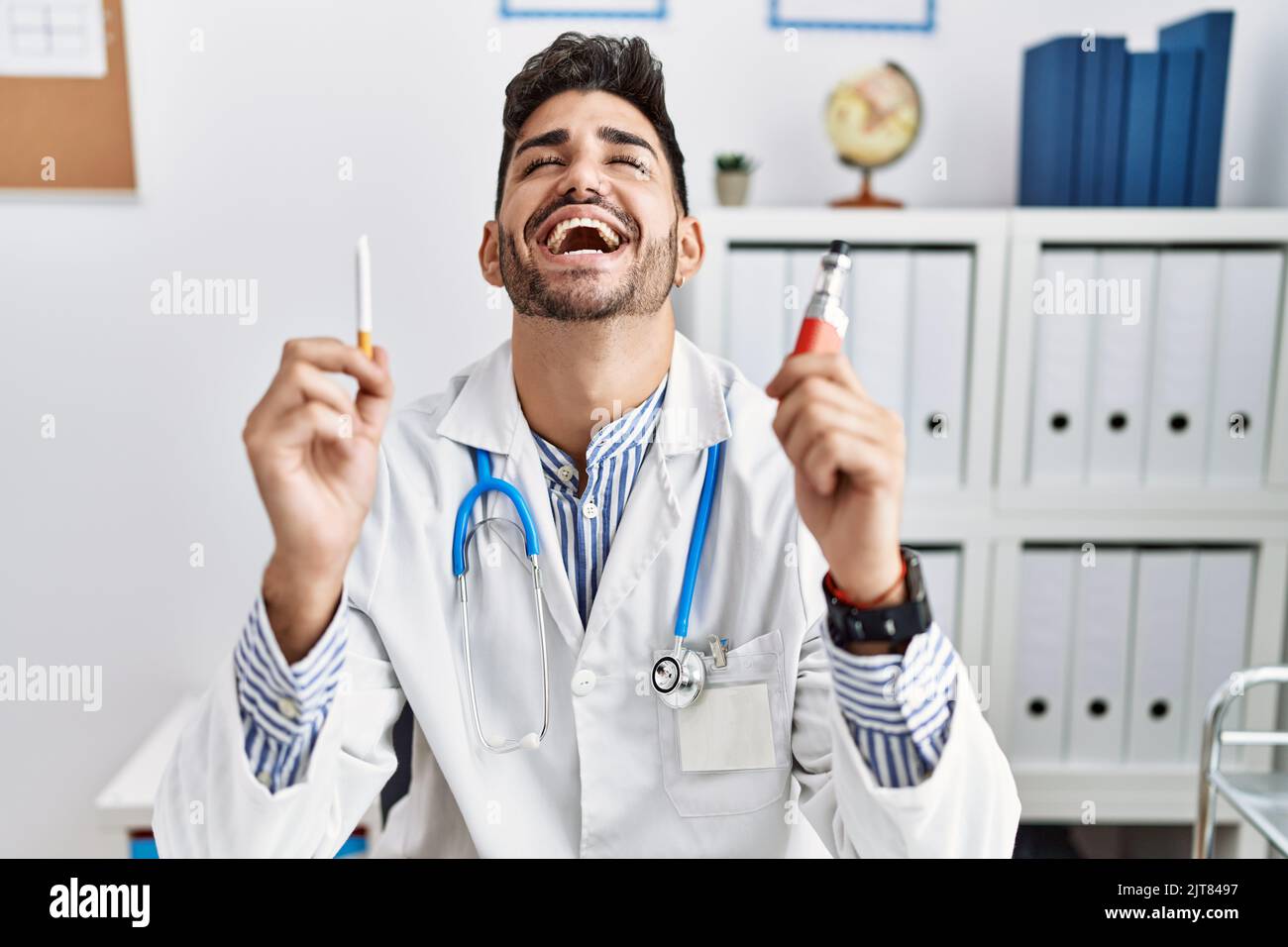 Young doctor man holding electronic cigarette at medical clinic smiling ...