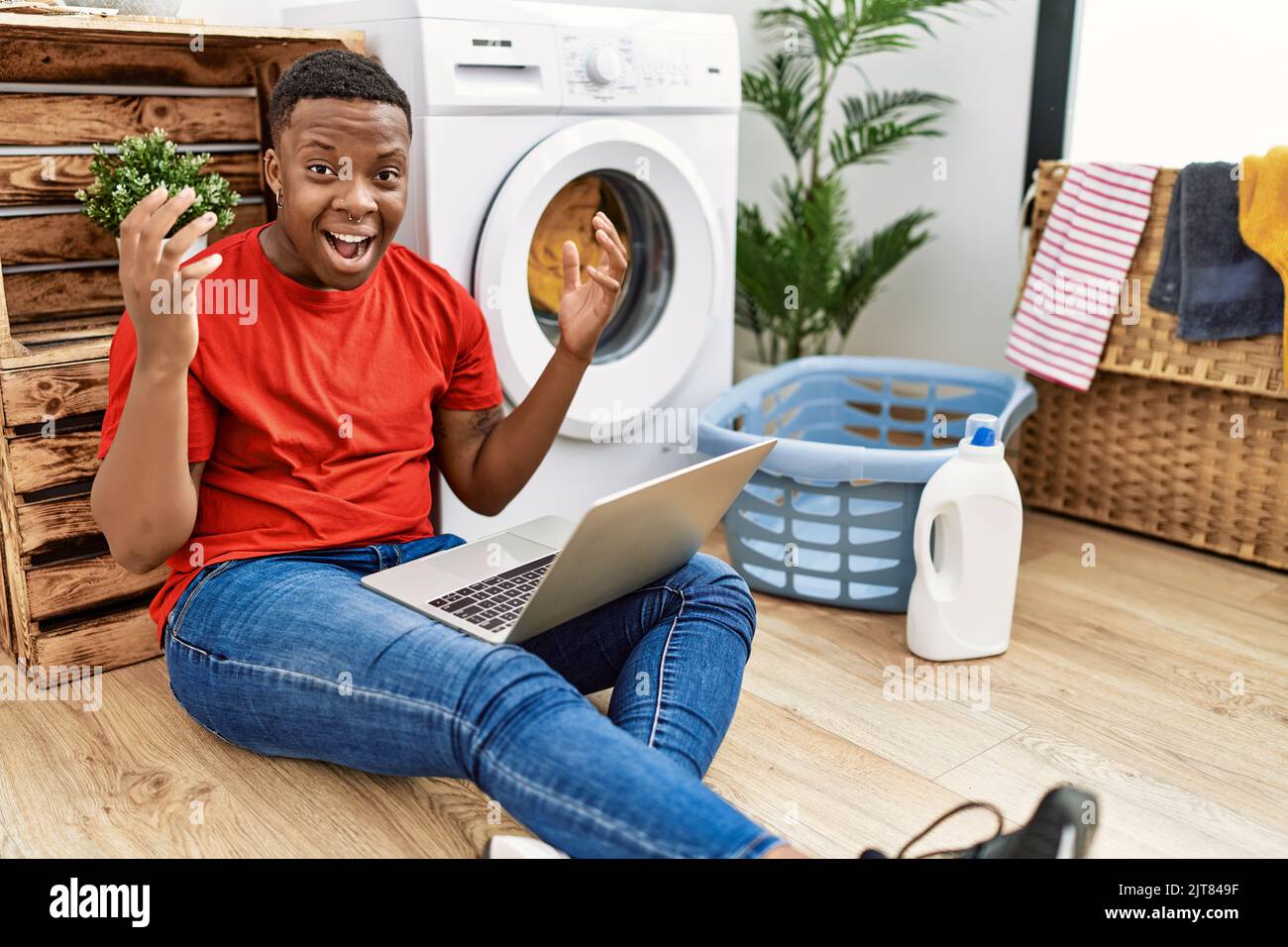 Young african man doing laundry and using computer celebrating crazy ...