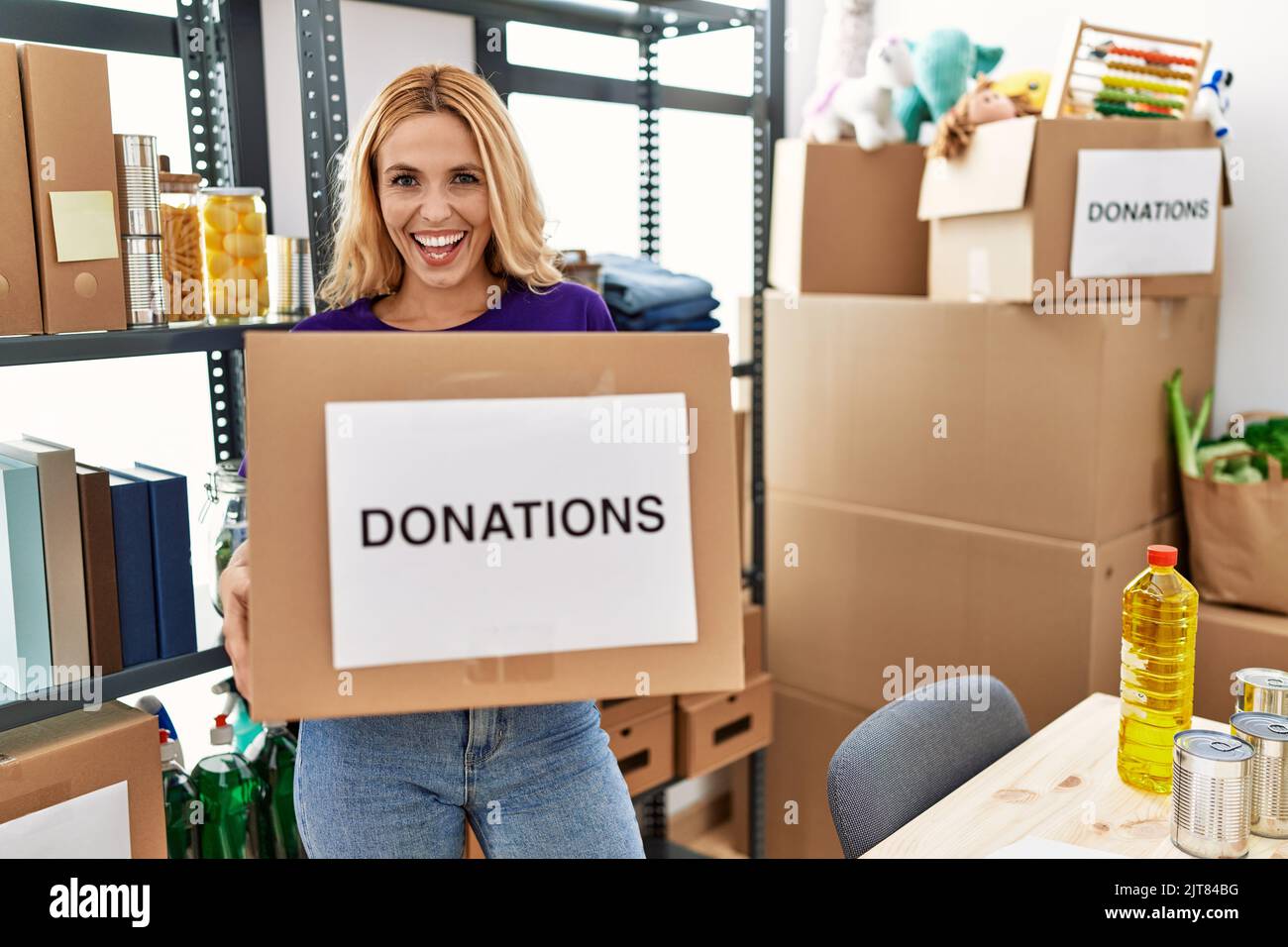 Beautiful blonde woman volunteer holding donations box smiling and ...