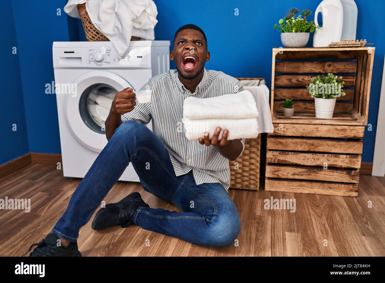 African american man holding clean laundry and laundry powder angry and ...