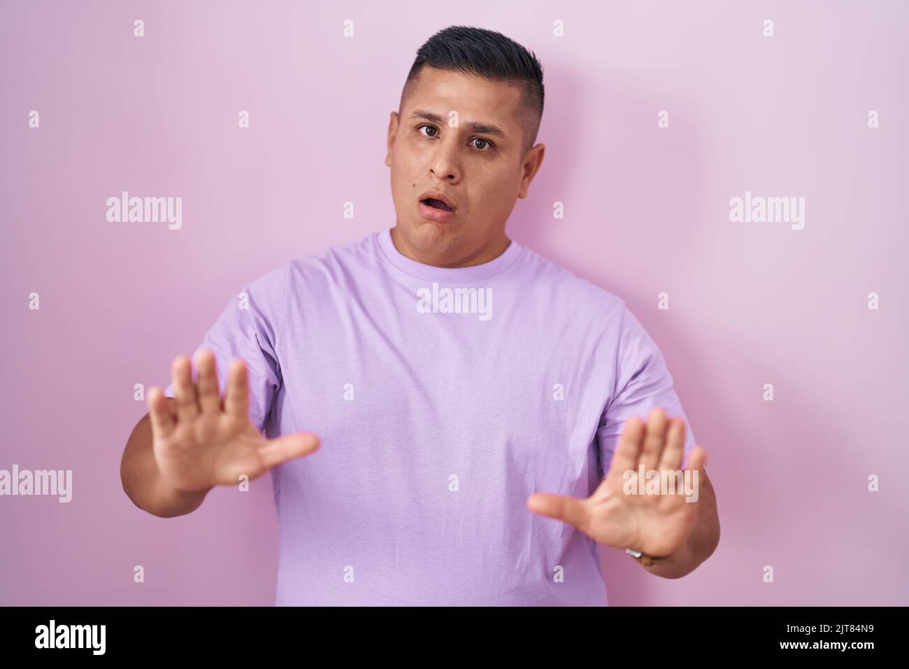 Young hispanic man standing over pink background moving away hands ...