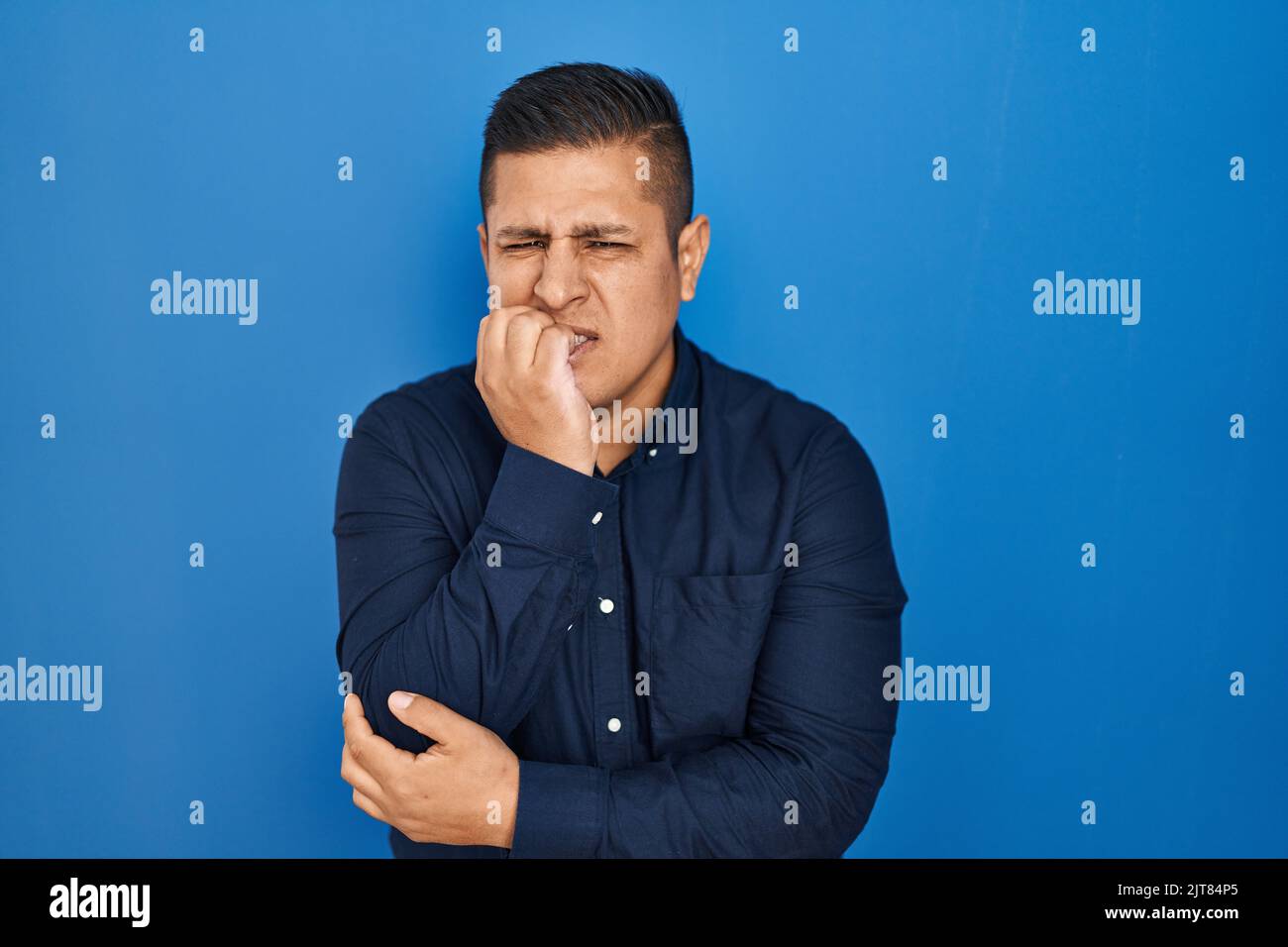 Hispanic young man standing over blue background looking stressed and ...