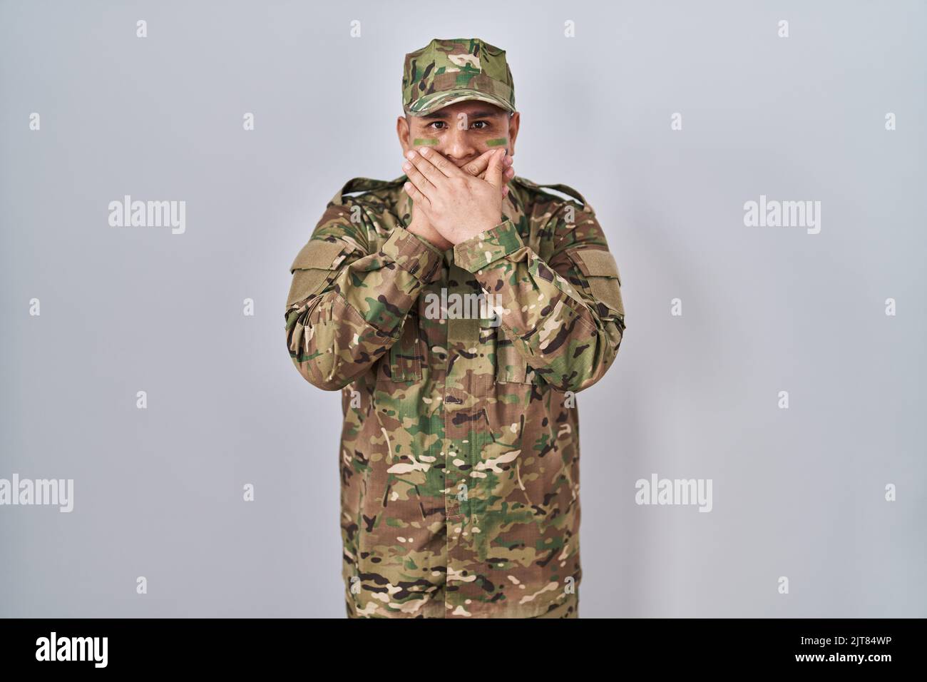 Hispanic young man wearing camouflage army uniform shocked covering ...
