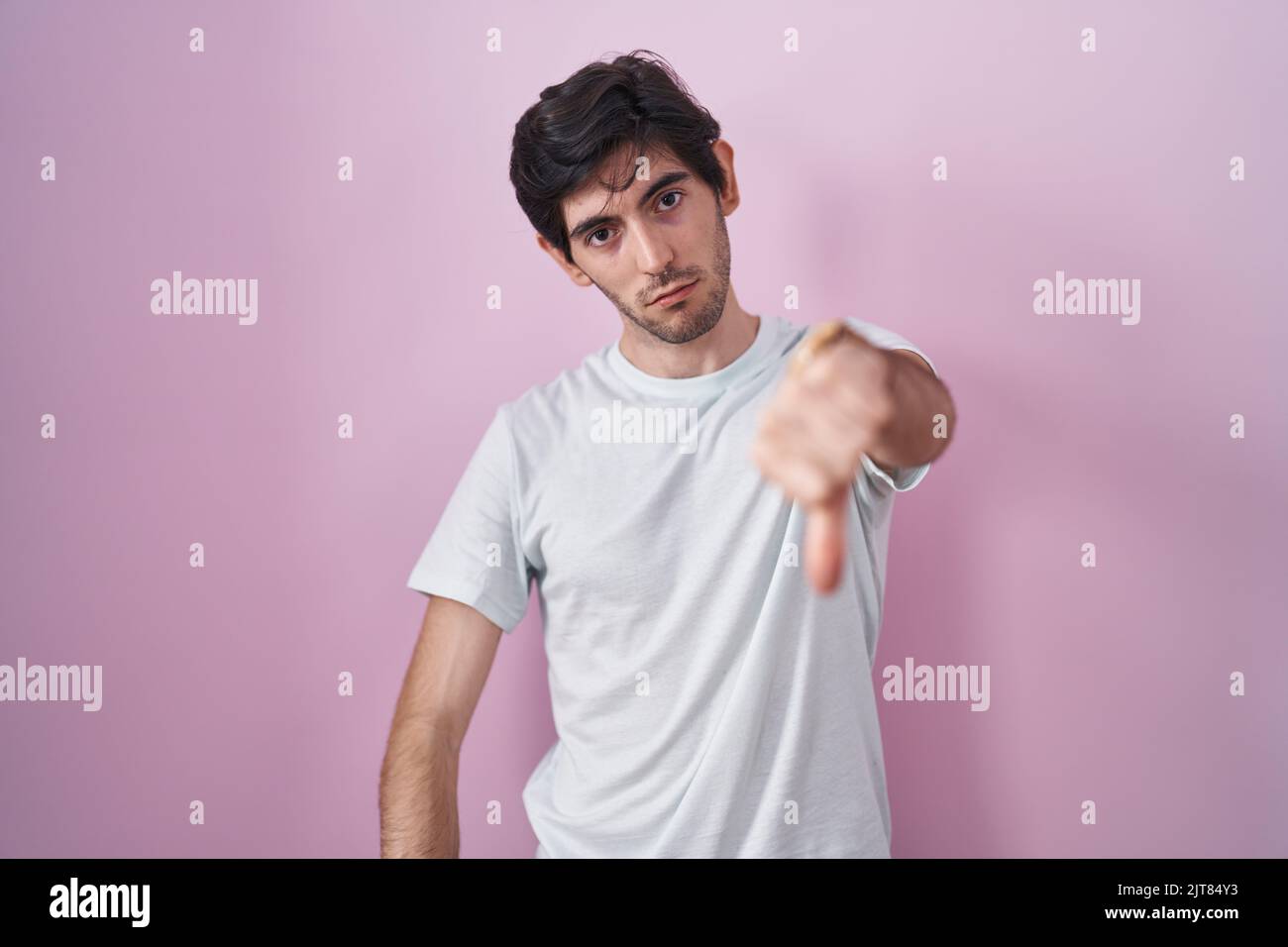 Young hispanic man standing over pink background looking unhappy and ...