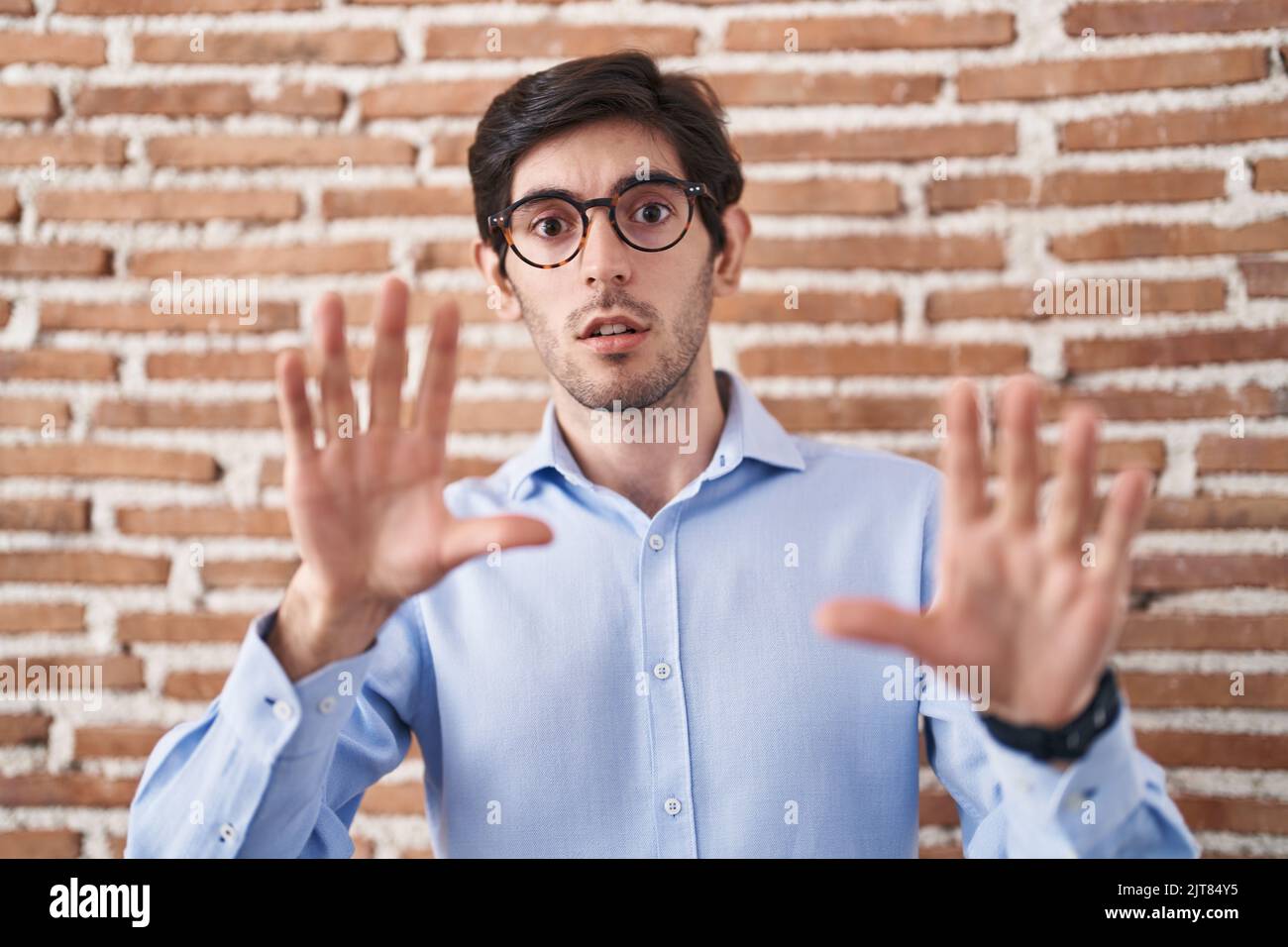 Young hispanic man standing over brick wall background afraid and ...
