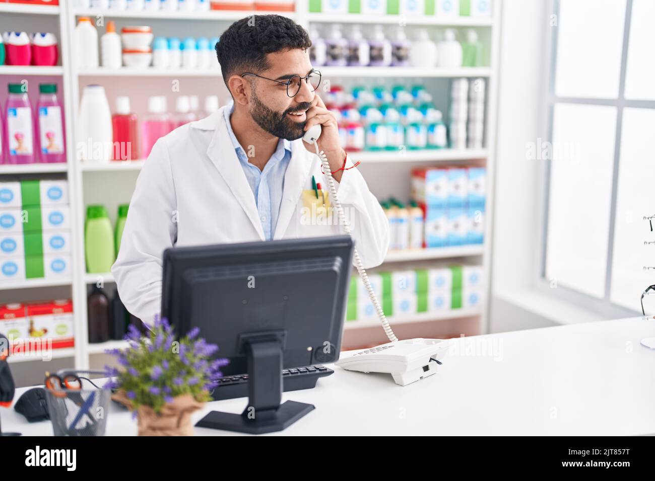 Young arab man pharmacist talking on telephone using computer at ...