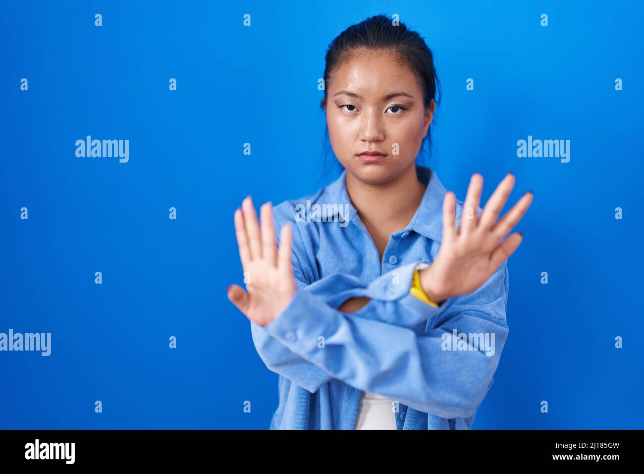 Asian Young Woman Standing Over Blue Background Rejection Expression