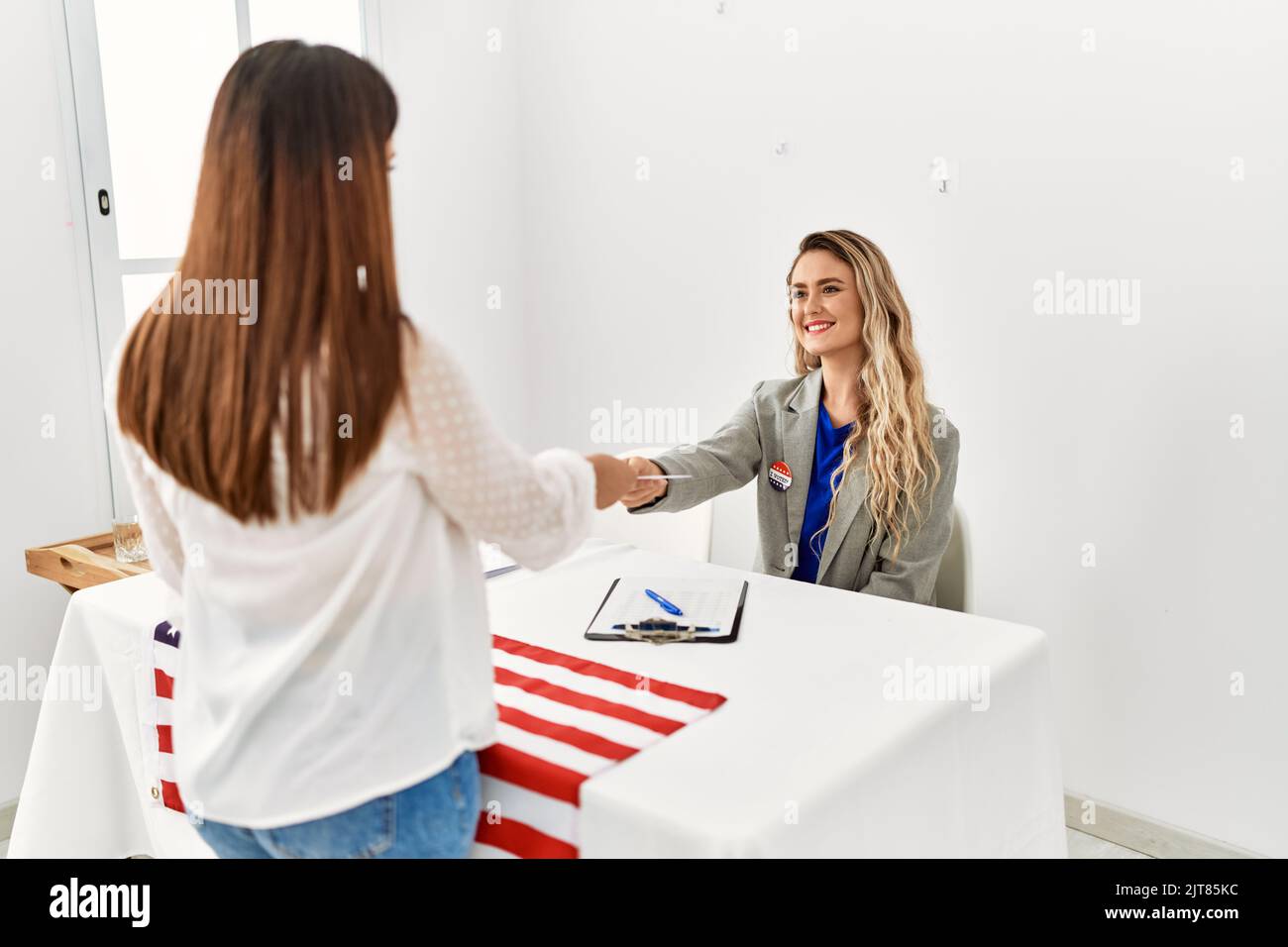 Young american voter woman giving party vote to electoral table worker ...