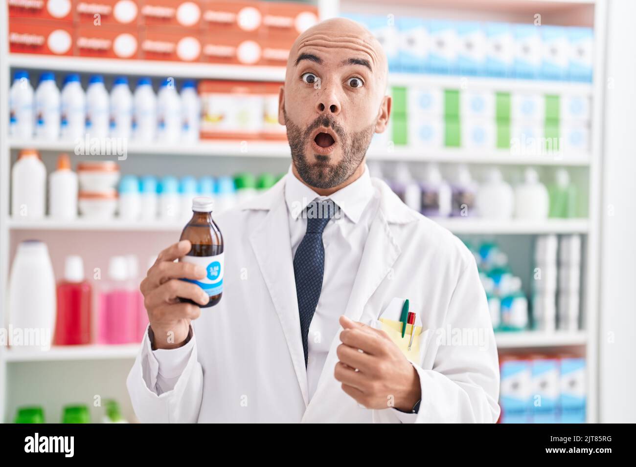 Middle age bald man working at pharmacy drugstore holding syrup scared ...