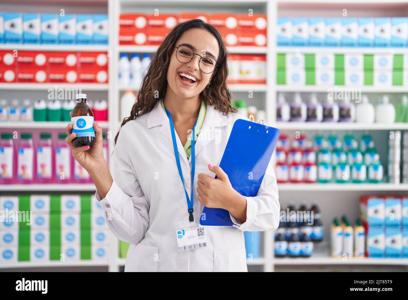Young hispanic woman working at pharmacy drugstore holding syrup ...