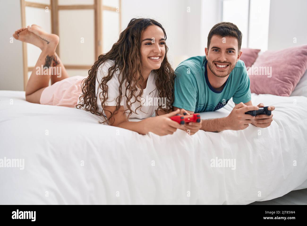 Young hispanic couple playing video game lying on bed at bedroom Stock ...