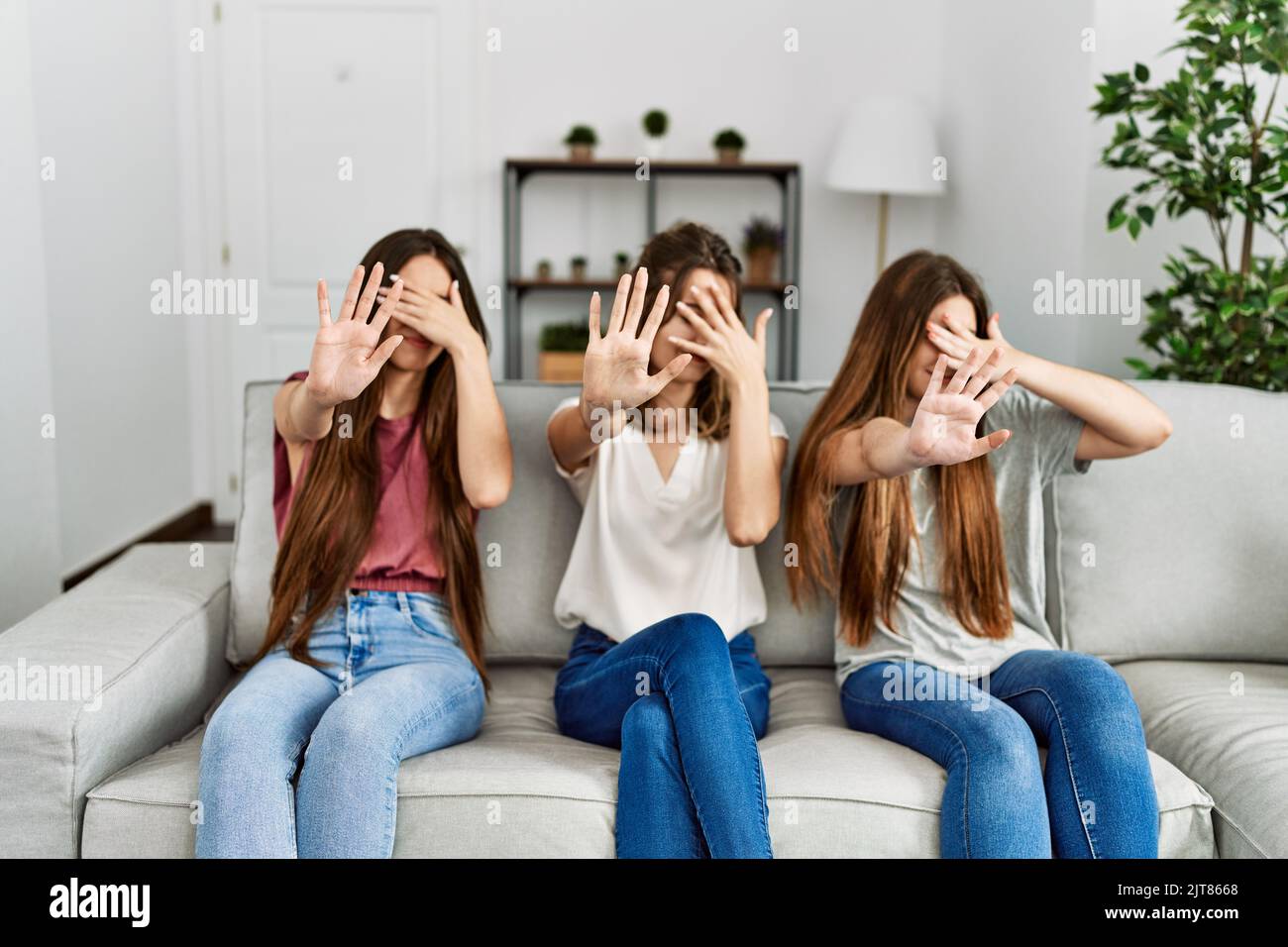 Group of three hispanic girls sitting on the sofa at home covering eyes ...