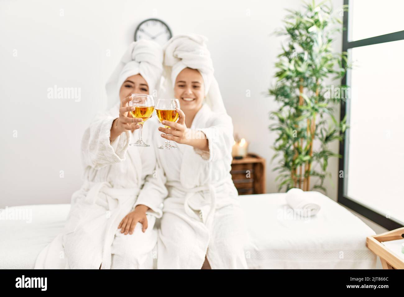 Woman couple wearing bathrobe toasting with champagne sitting on ...