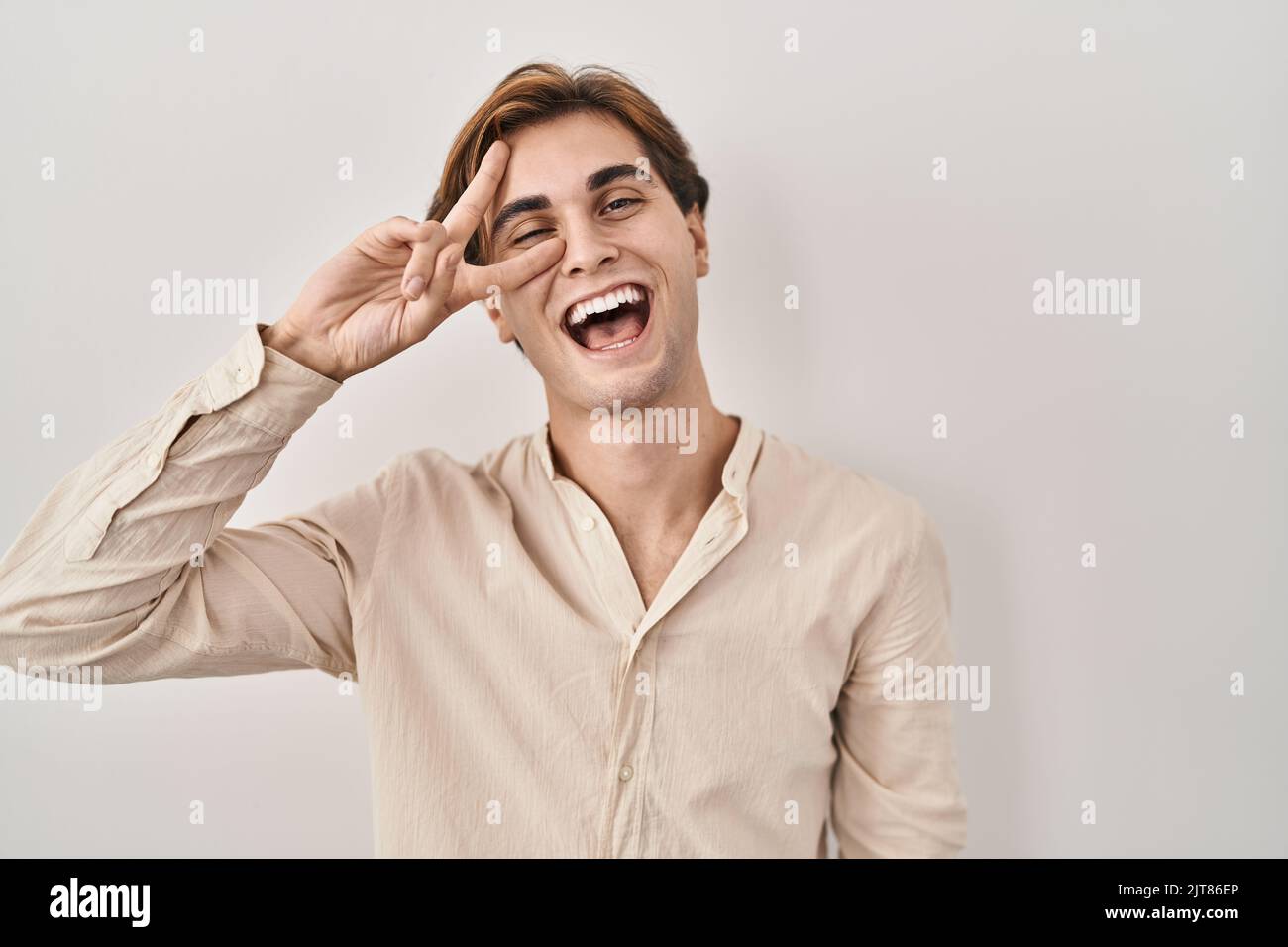 Young man standing over isolated background doing peace symbol with ...