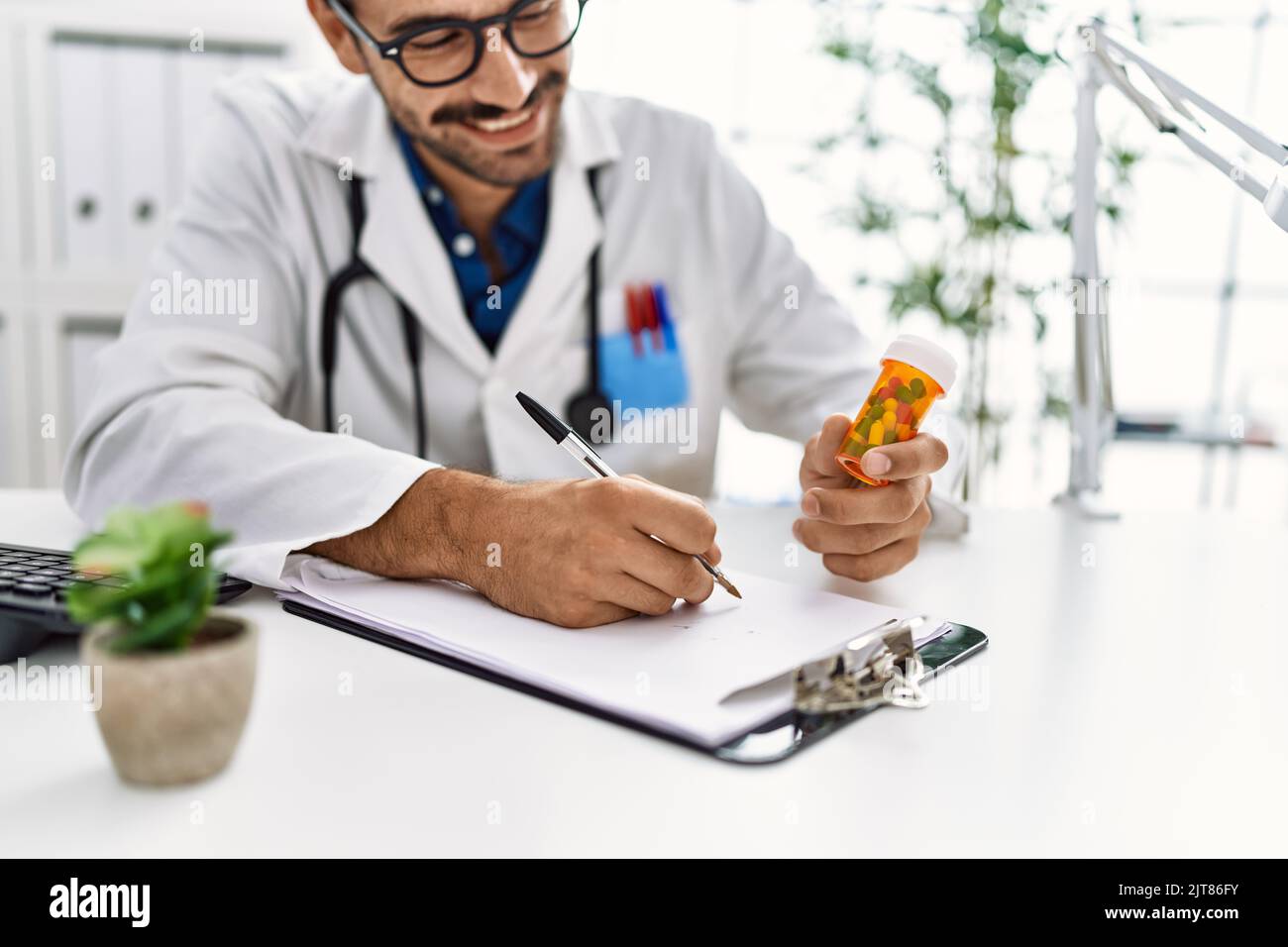 Handsome hispanic man working as doctor writing pills presciption at ...