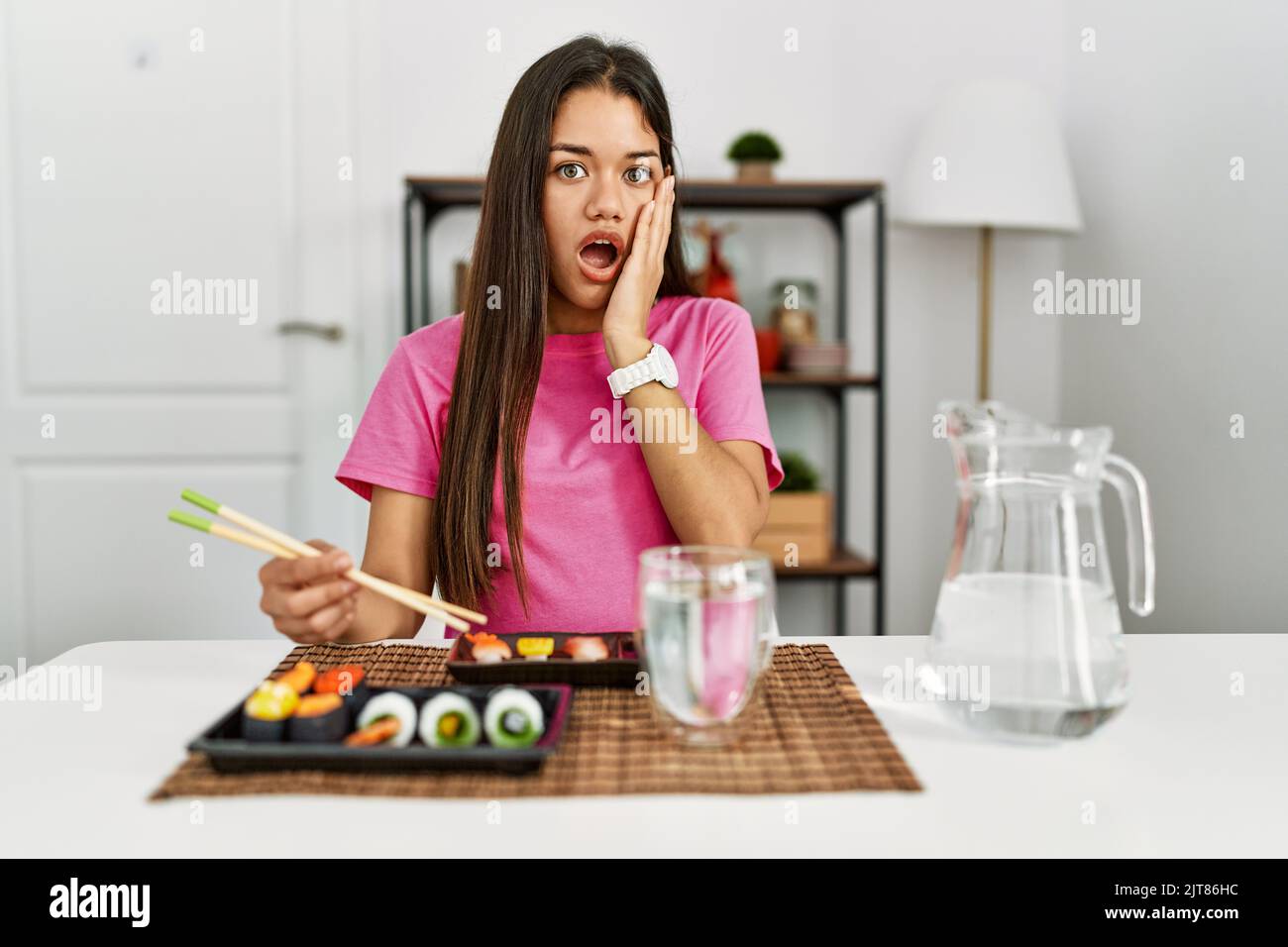 Young brunette woman eating sushi using chopsticks afraid and shocked ...