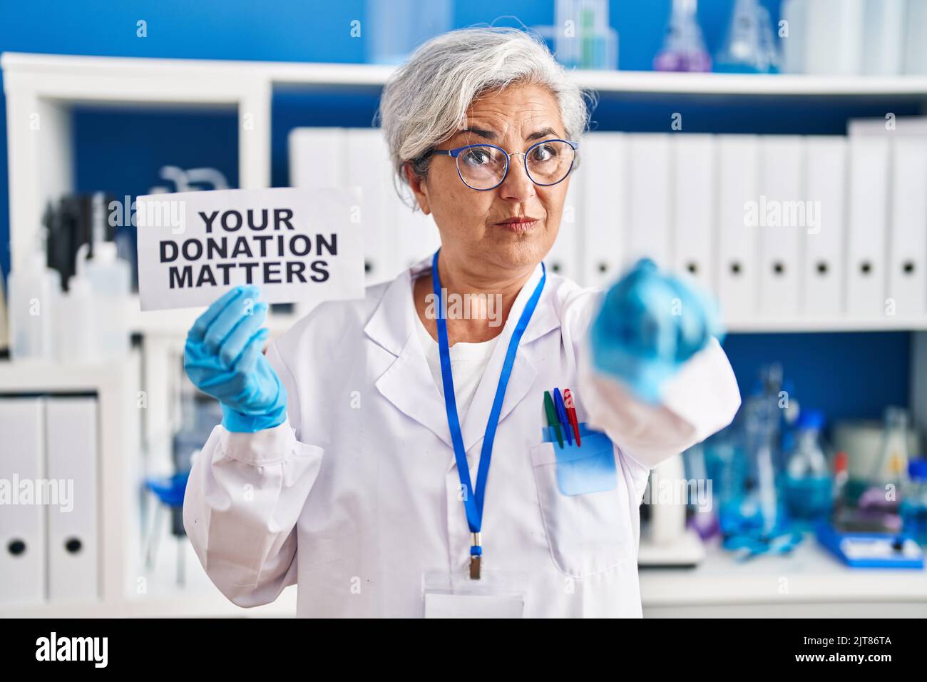 Middle age woman with grey hair working at scientist laboratory holding your donation matters ...