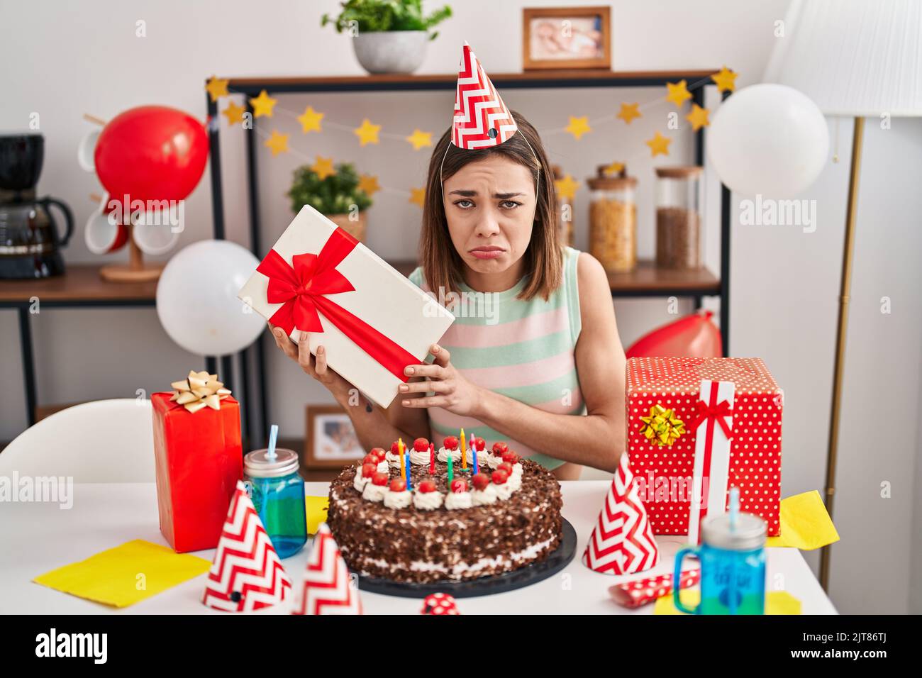 Hispanic woman celebrating birthday with cake holding gift depressed ...
