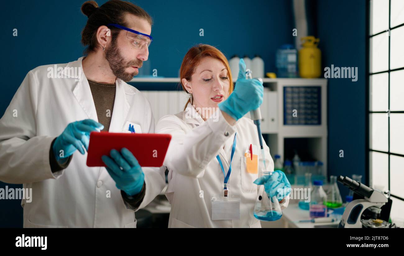 Man and woman wearing sciencist uniform using touchpad at laboratory ...
