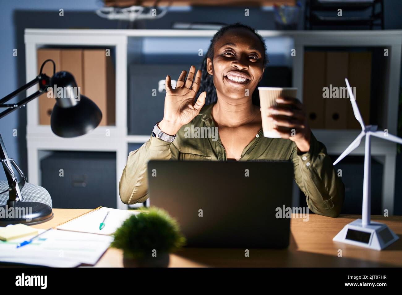 African woman working using computer laptop at night waiving saying ...