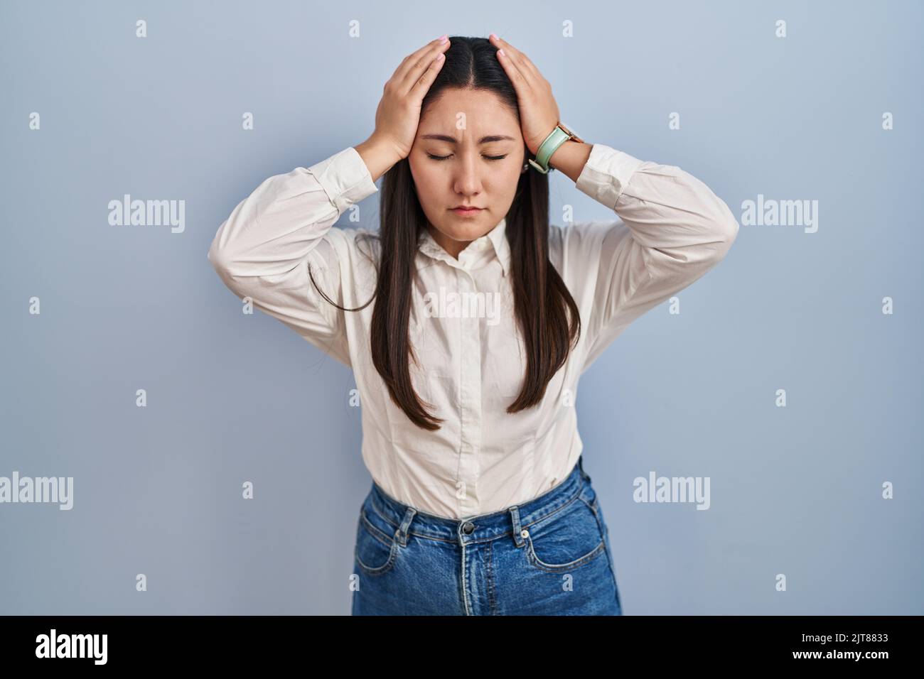 Young latin woman standing over blue background suffering from headache ...