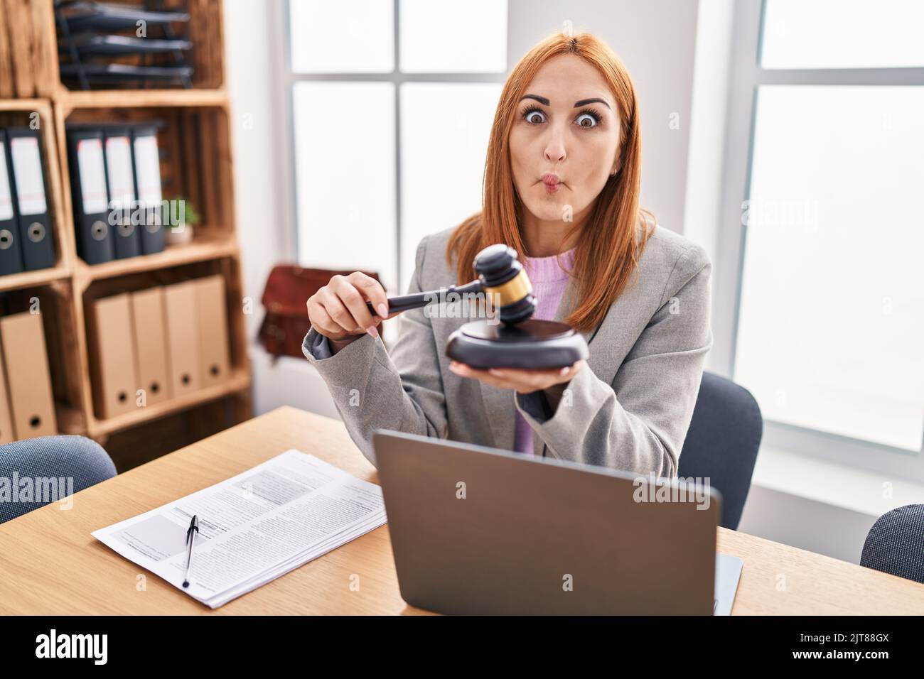 Young business woman using gavel making fish face with mouth and ...