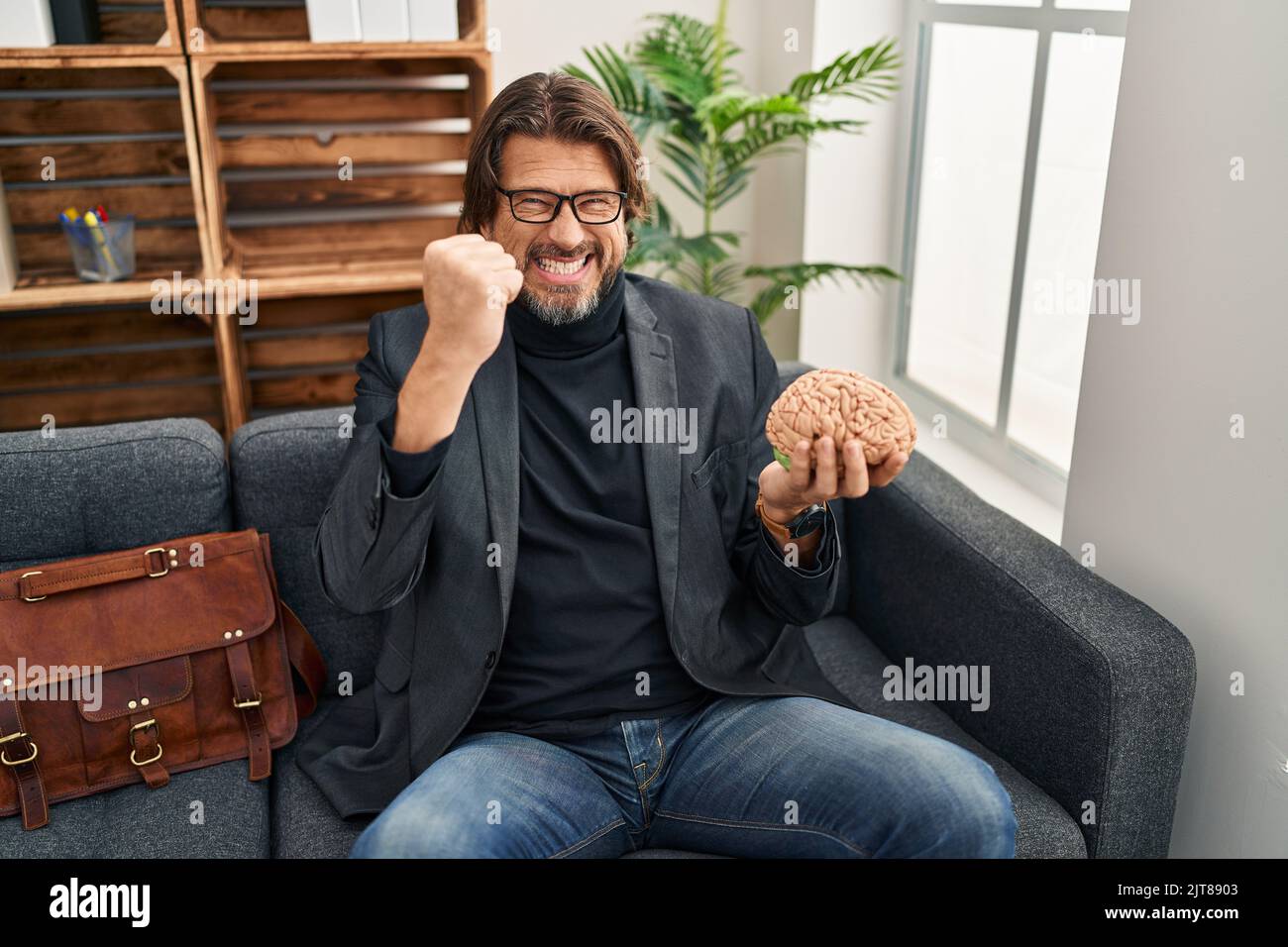 Handsome middle age man at consultation office holding brain annoyed ...
