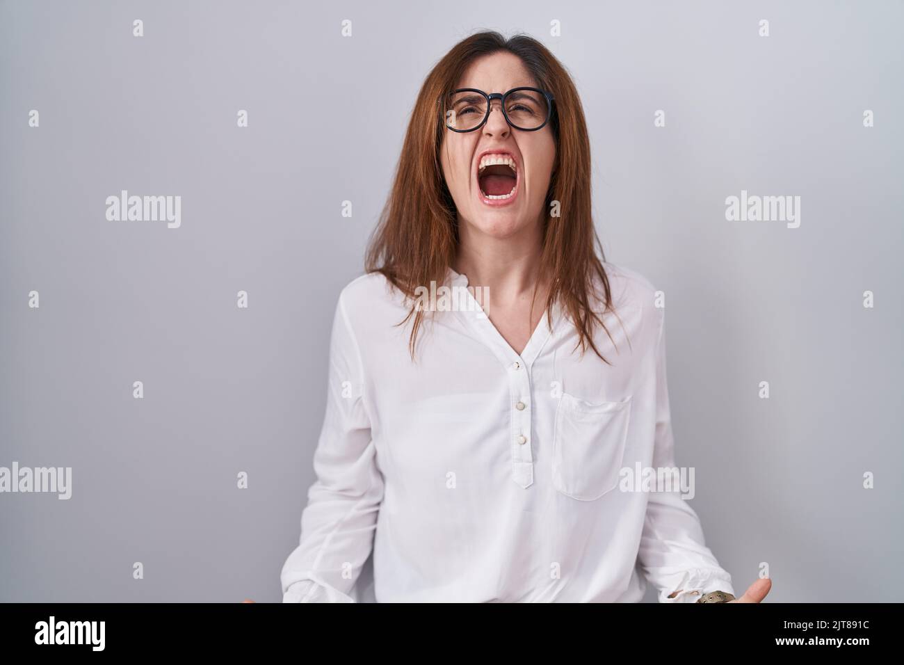 Brunette woman standing over white isolated background angry and mad ...