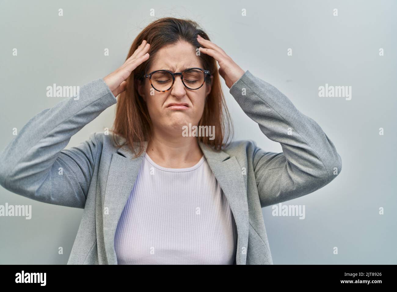 Brunette woman standing over grey background with hand on head ...