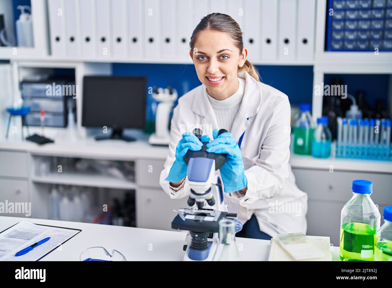 Young woman scientist smiling confident using microscope at laboratory ...