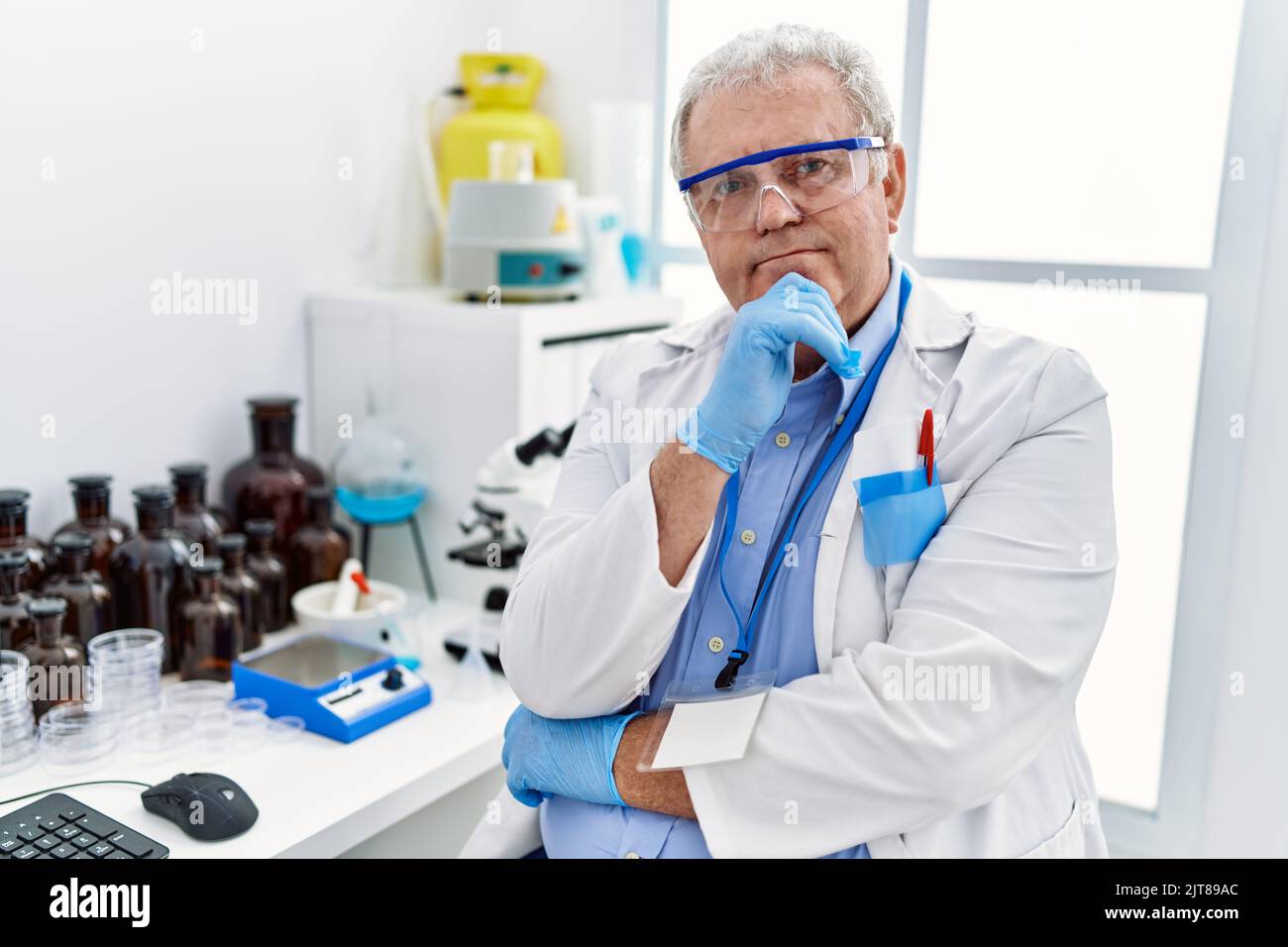 Middle age grey-haired man wearing scientist uniform with arms crossed ...