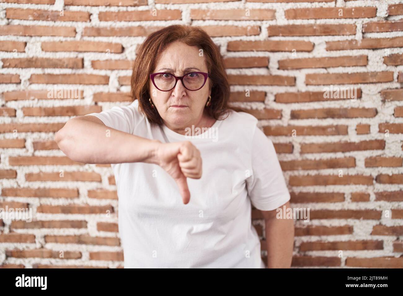 Senior Woman With Glasses Standing Over Bricks Wall Looking Unhappy And