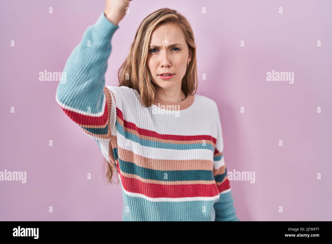 Young blonde woman standing over pink background angry and mad raising ...