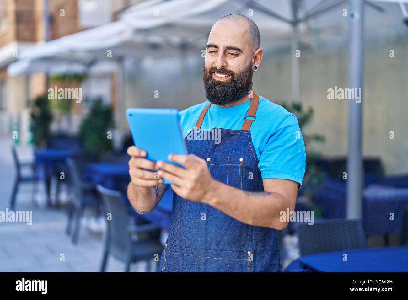 Young bald man waiter smiling confident using touchpad at coffee shop ...