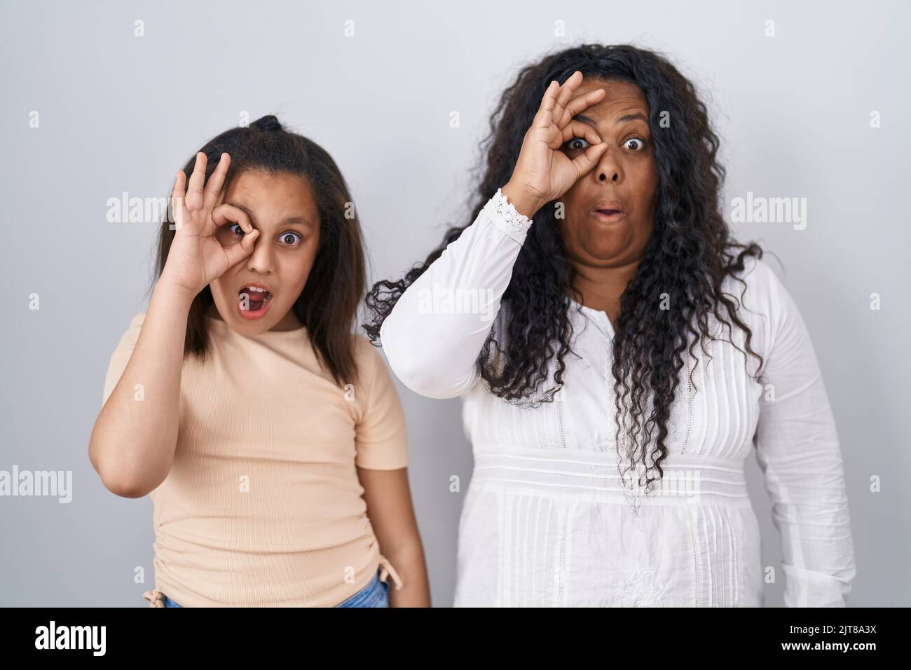 Mother and young daughter standing over white background doing ok ...