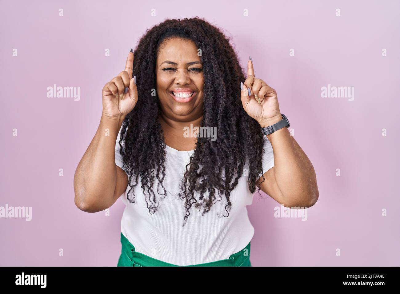 Plus size hispanic woman standing over pink background smiling amazed ...