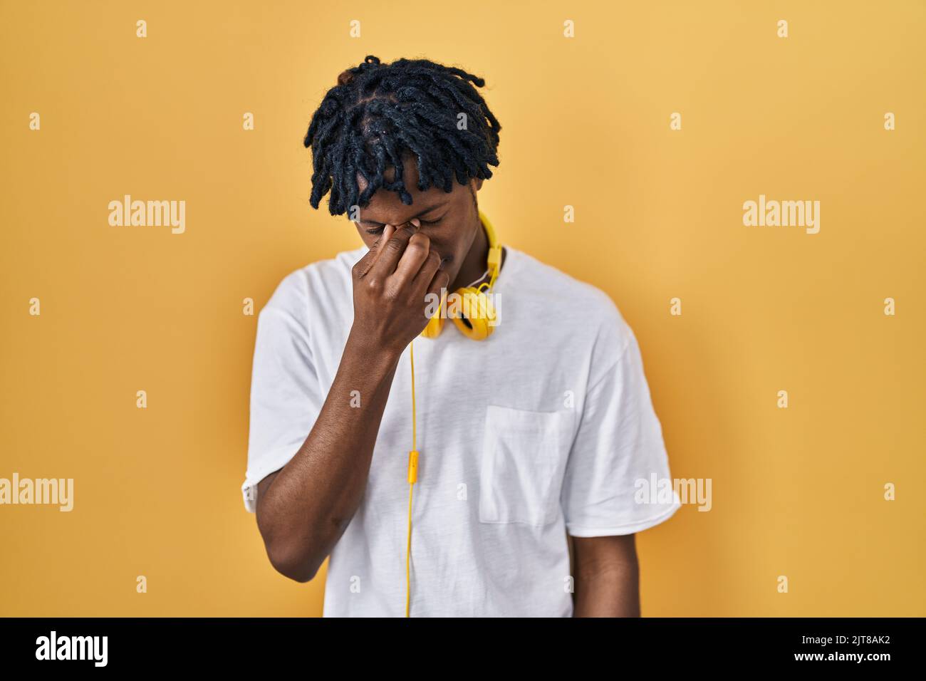 Young african man with dreadlocks standing over yellow background tired ...