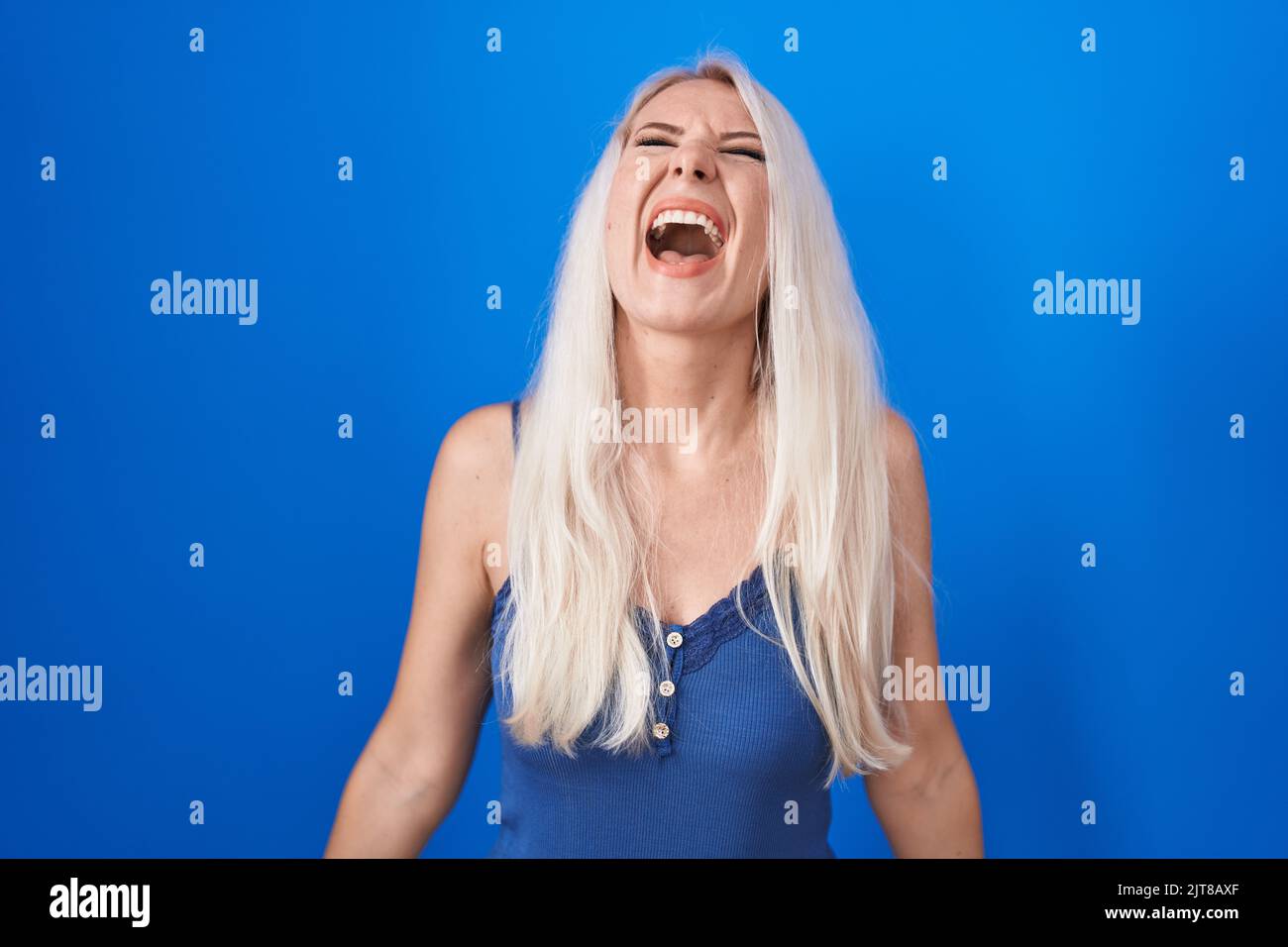Caucasian woman standing over blue background angry and mad screaming ...