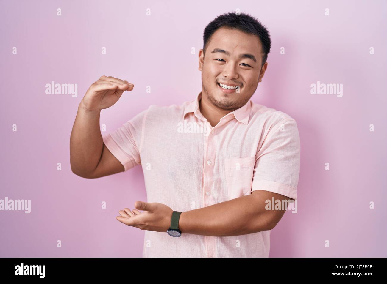 Chinese young man standing over pink background gesturing with hands ...