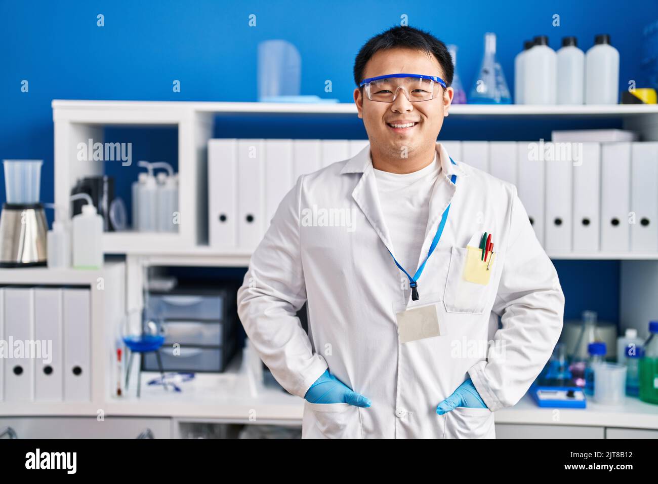Young chinese man wearing scientist uniform standing at laboratory ...