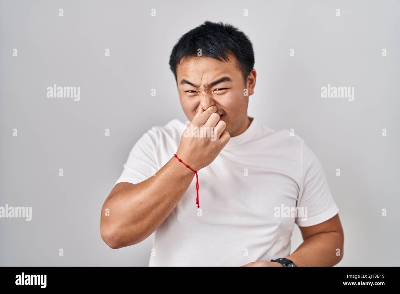 Young chinese man standing over white background smelling something ...