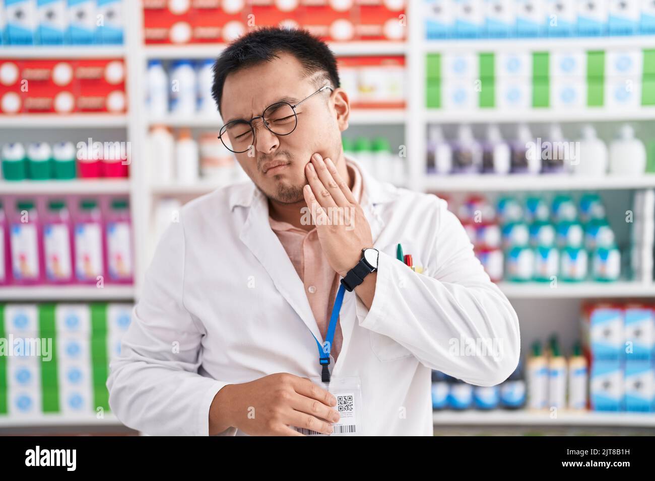 Chinese young man working at pharmacy drugstore touching mouth with ...